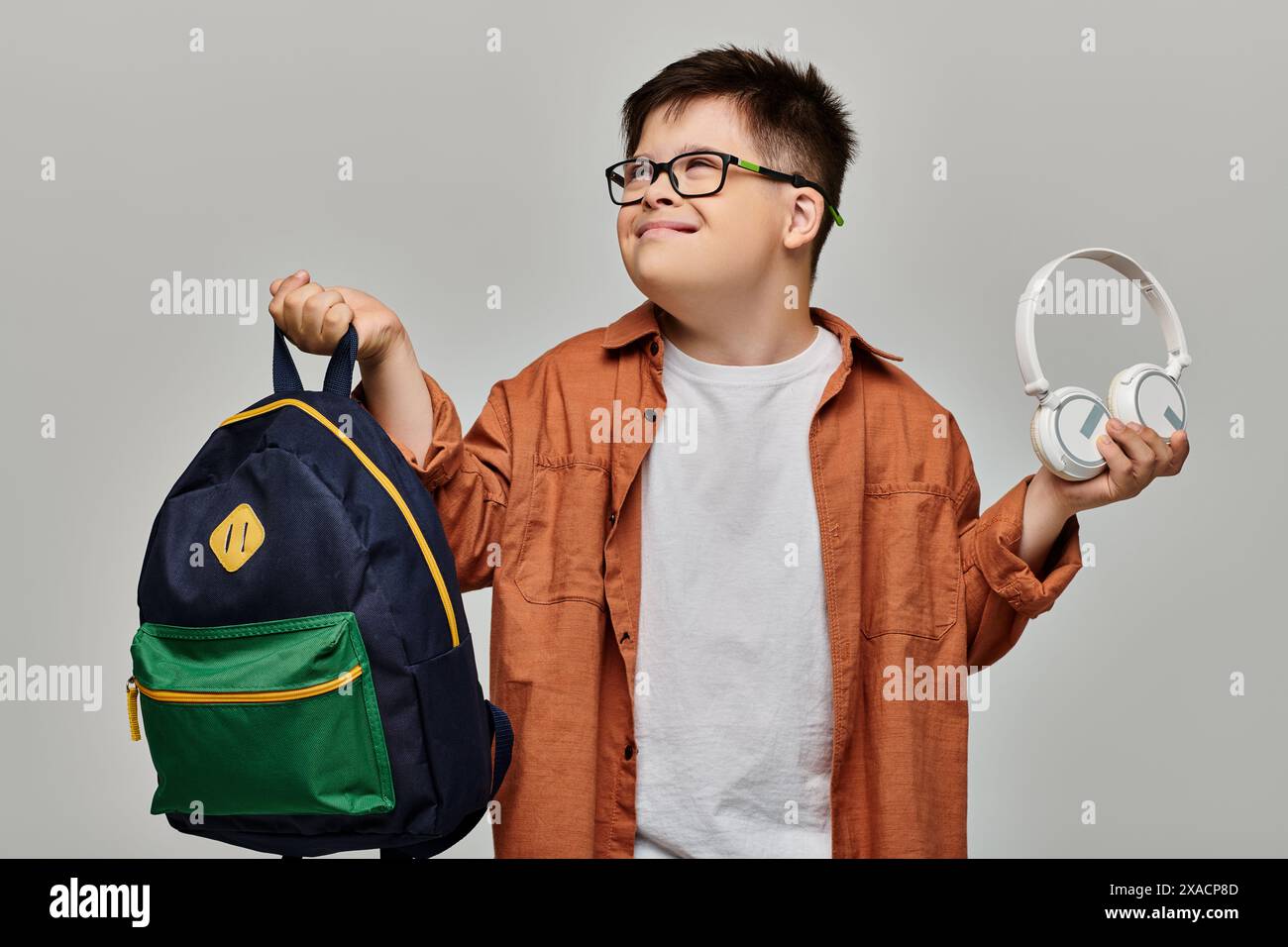 little kid with Down syndrome holds backpack and headphones Stock Photo ...