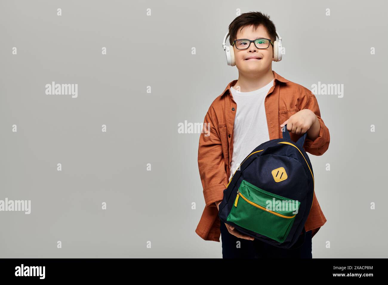 A little kid with Down syndrome holding a backpack and wearing ...