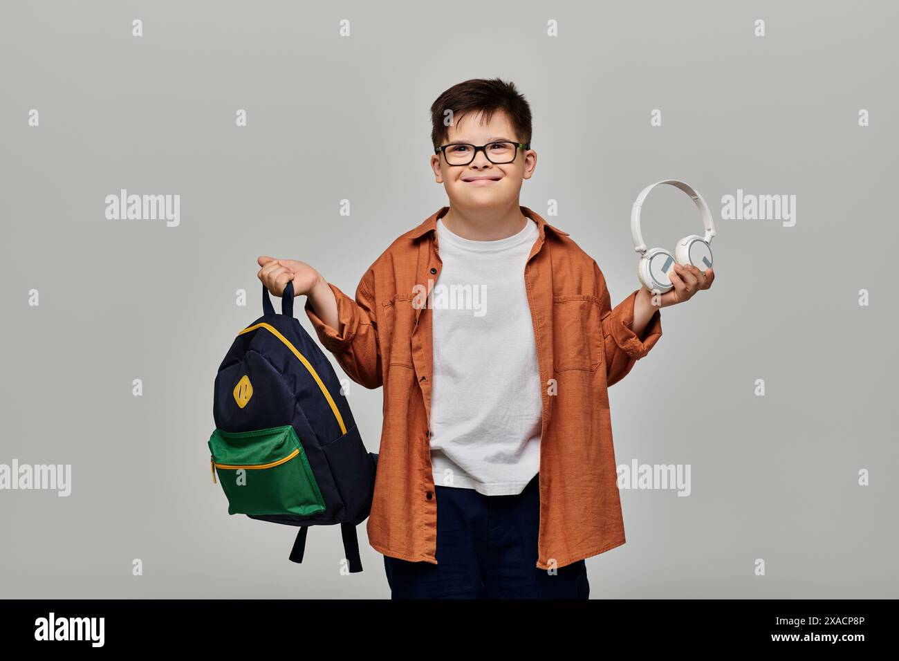 A little kid with Down syndrome holding a backpack and wearing ...