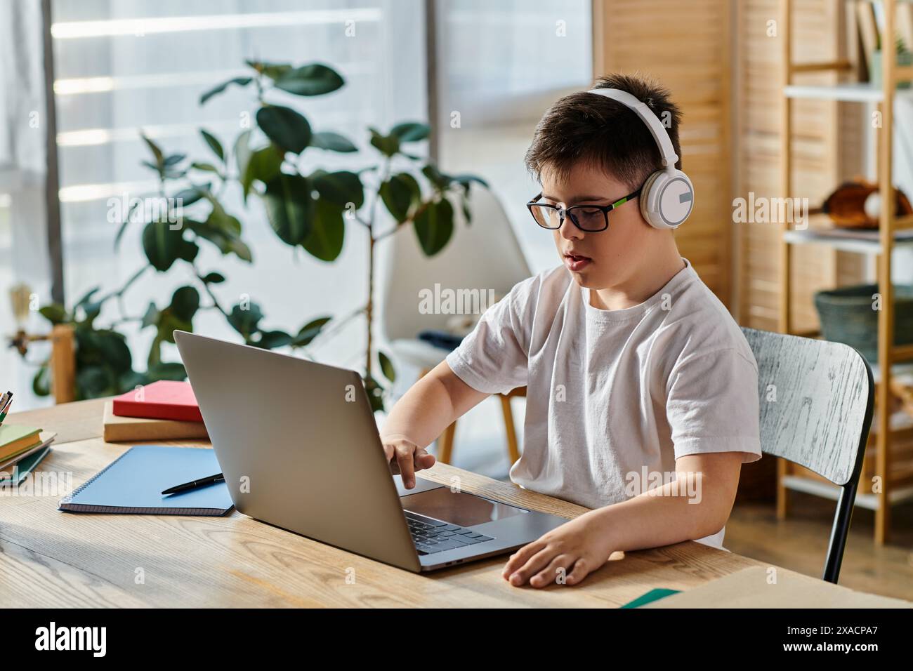 A kid with Down syndrome uses a laptop at home while wearing headphones ...