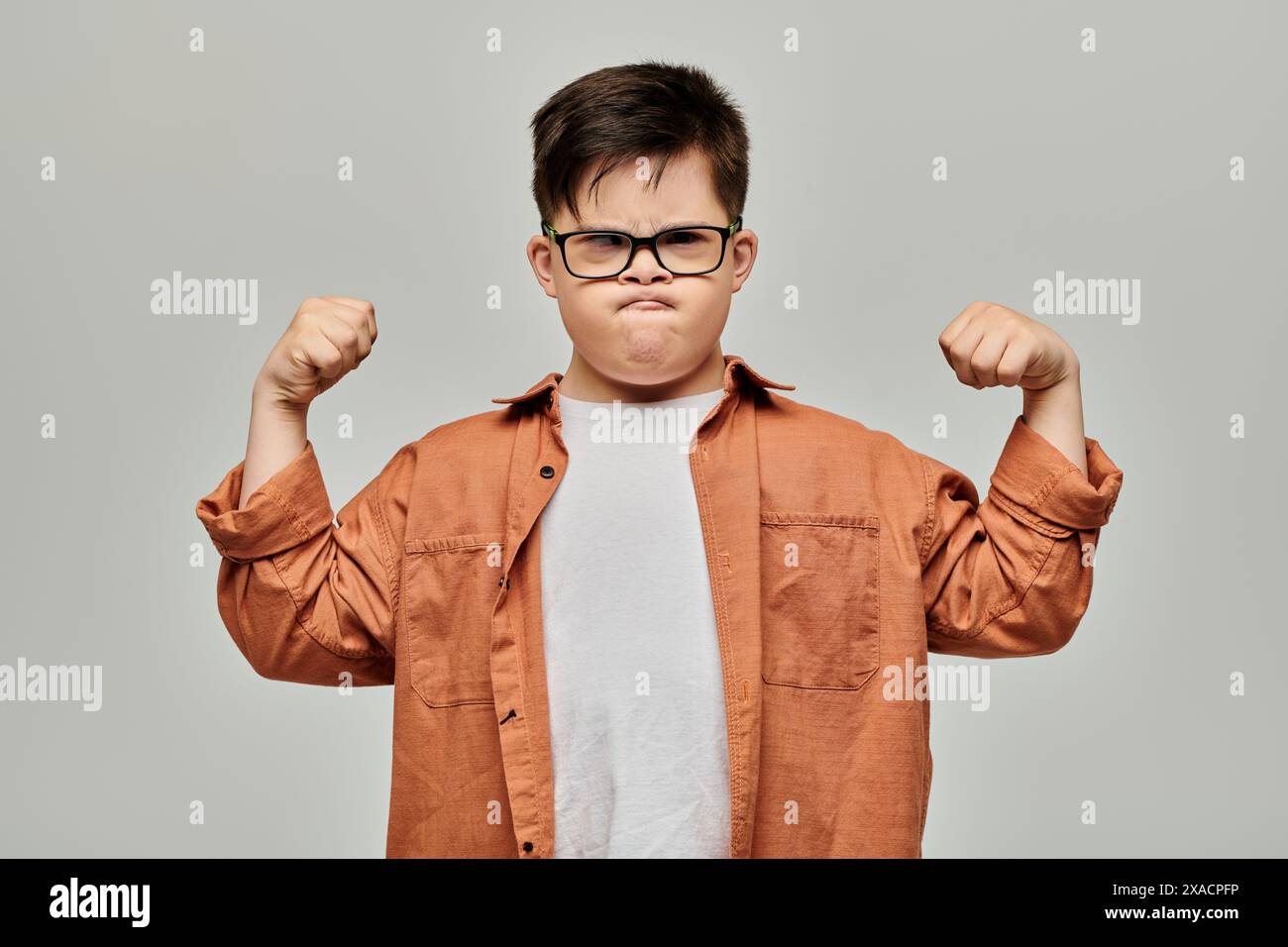 A little boy with Down syndrome with glasses flexes his muscles ...