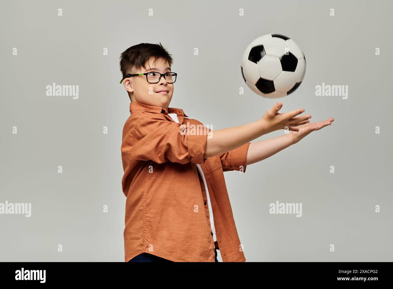 A charming child with Down syndrome balances a soccer ball on a grey ...