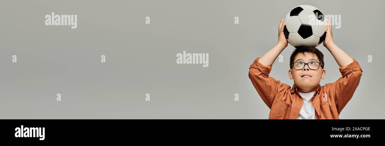 Little child with Down syndrome joyfully holds soccer ball above his ...