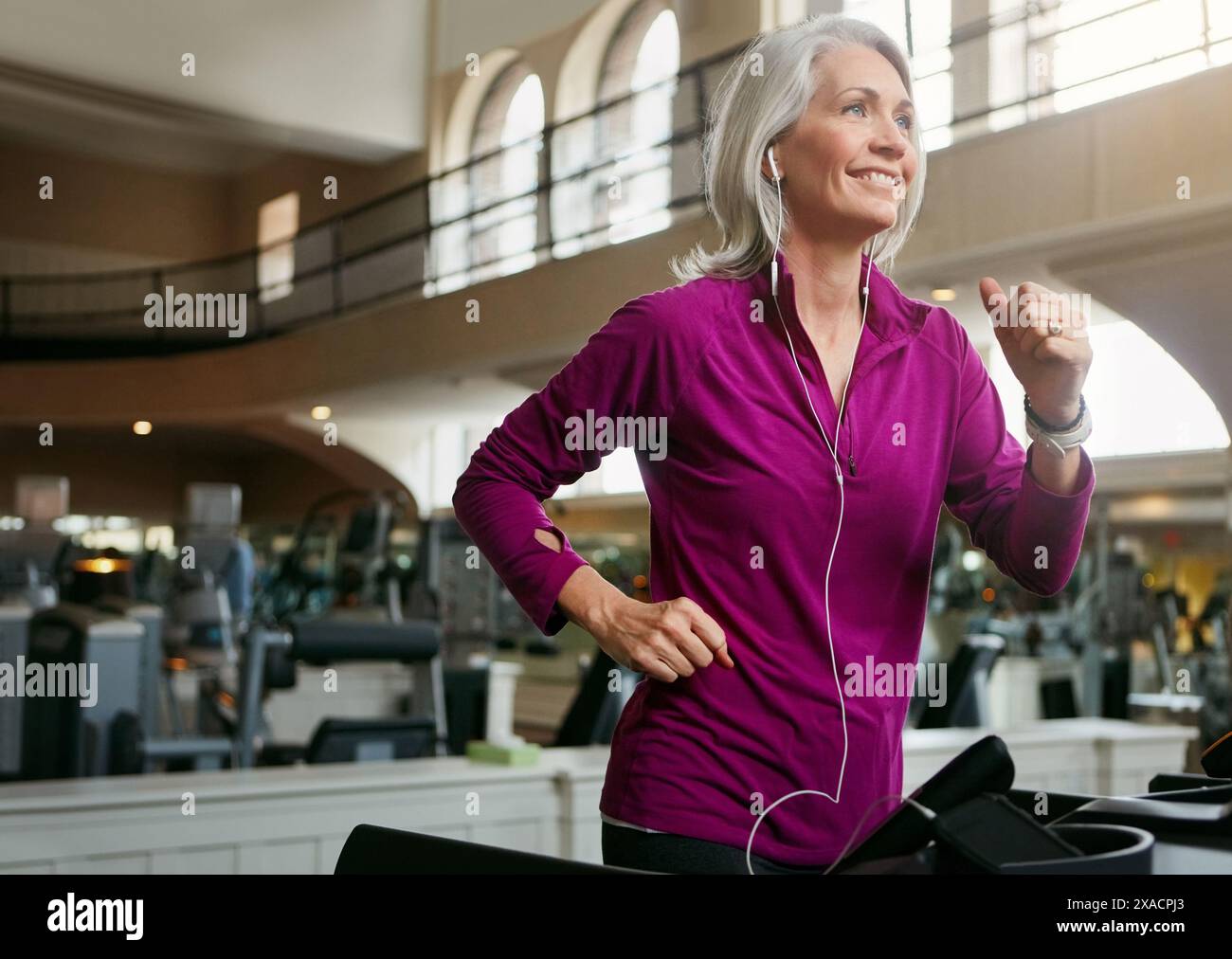 Senior woman, running on treadmill and smile for music in gym club ...