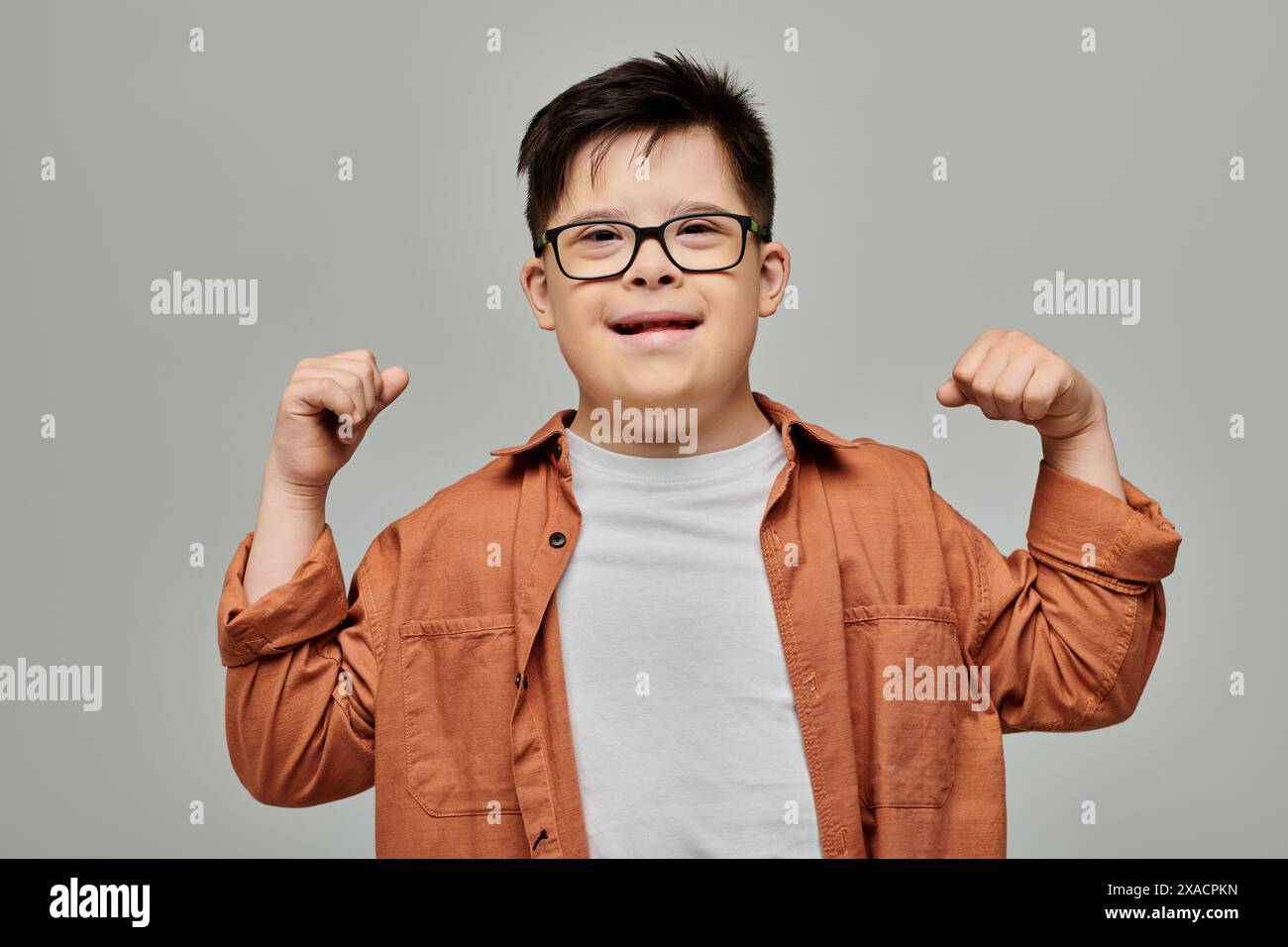 little kid with Down syndrome flexing his arms proudly against a gray ...