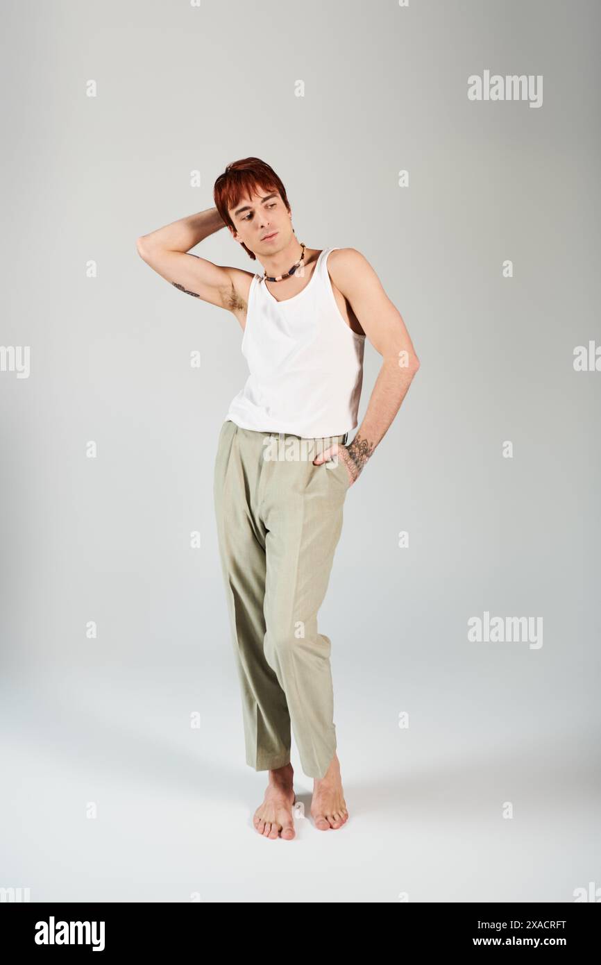 A stylish young man striking a pose in a white tank top and khaki pants ...