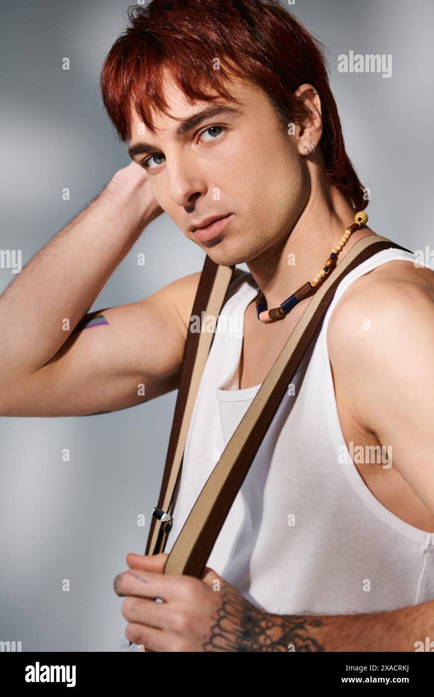 A stylish young man with red hair striking a pose in a white tank top ...