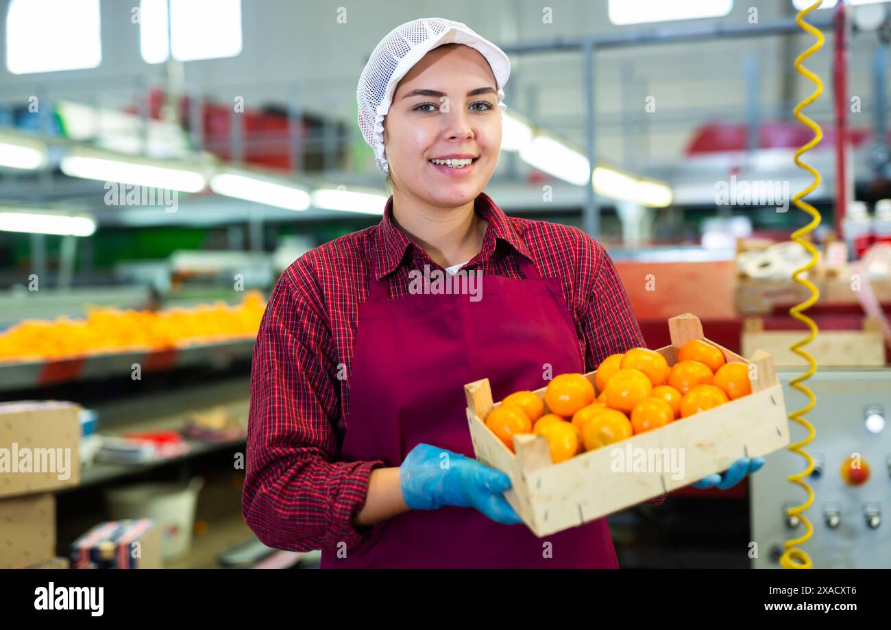 Glad positive female employee in colored uniforms hold a box of fresh ...