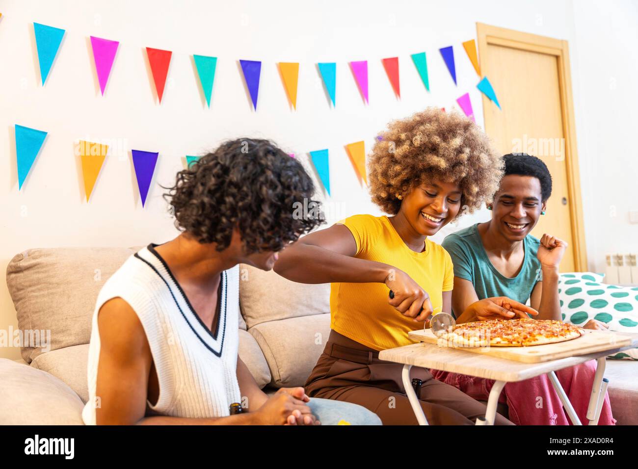 African woman cutting pizza in slices to share with multi-ethnic male ...