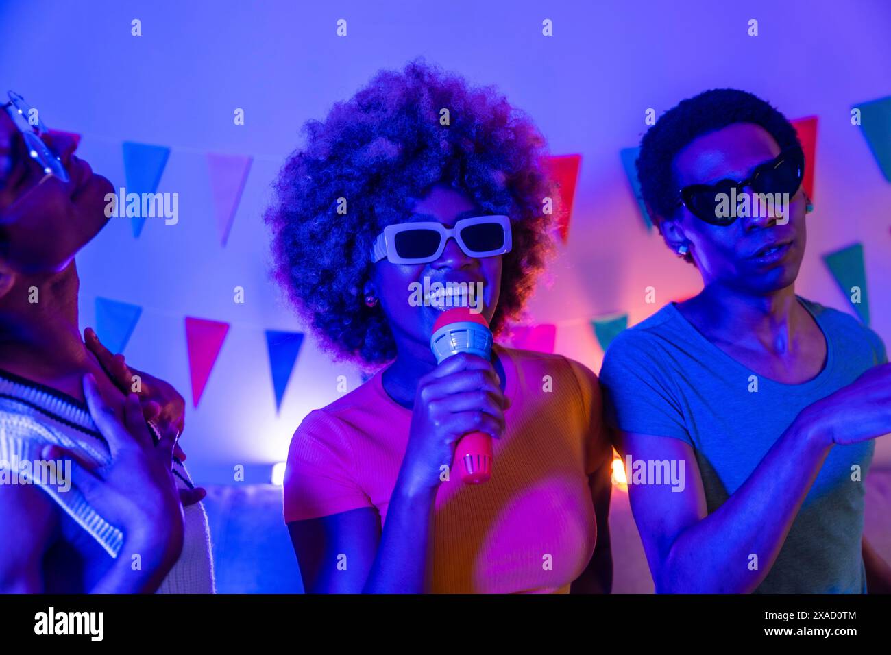 Cool afro woman singing karaoke with friends at home at night with blue ...