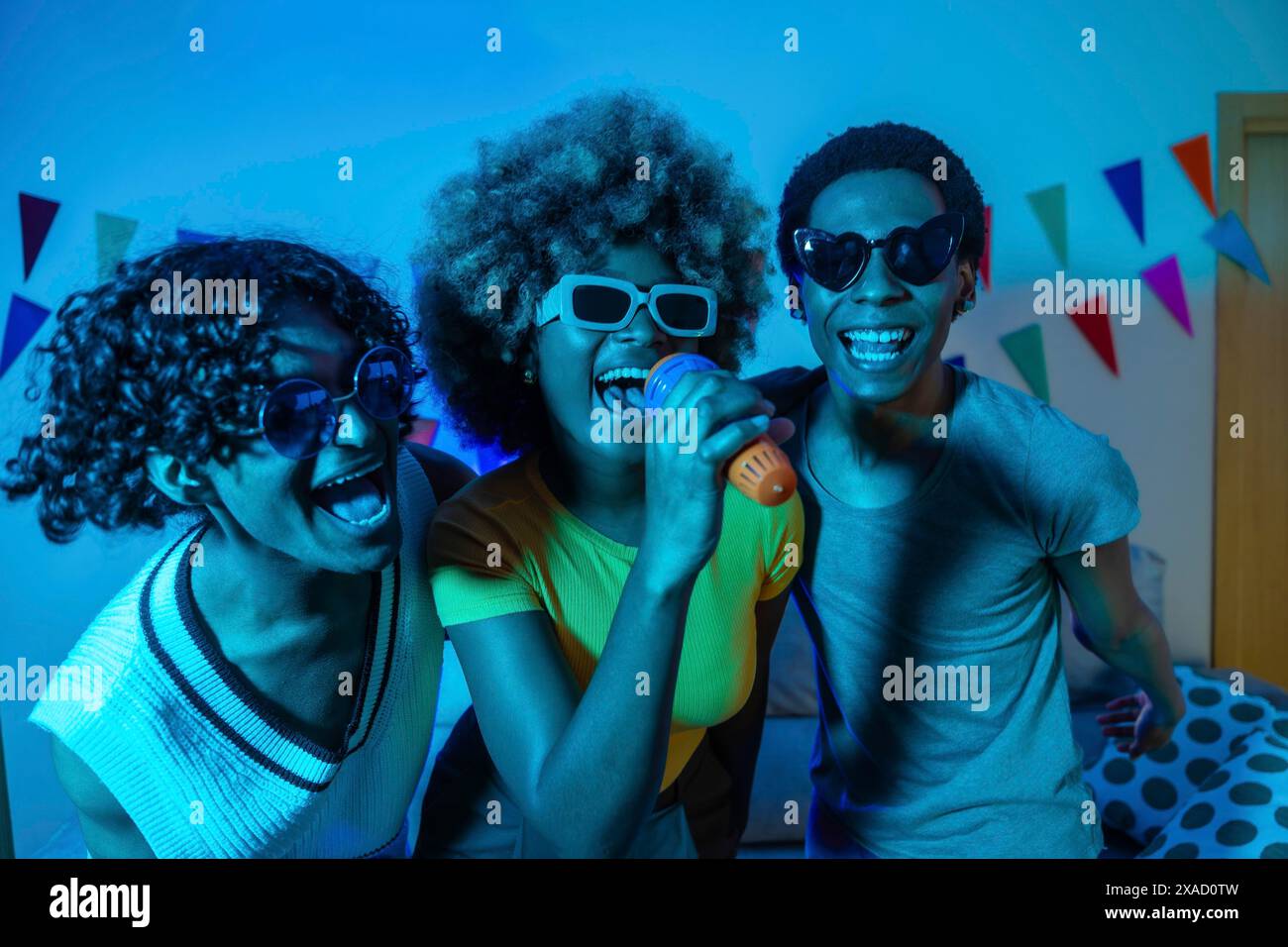 Multiracial friends singing karaoke partying at home at night with blue ...