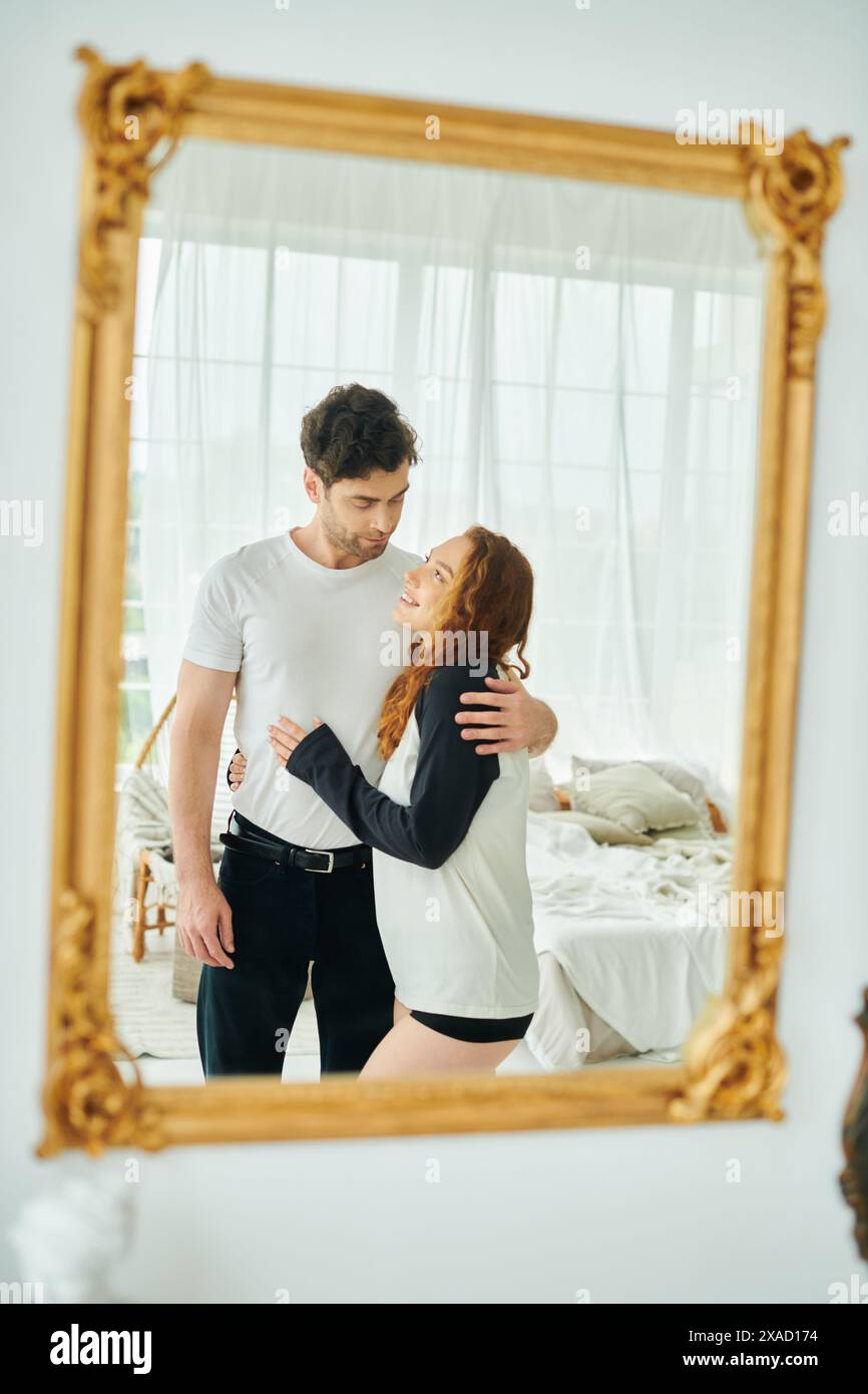 A man and woman standing together before a mirror, gazing at their ...