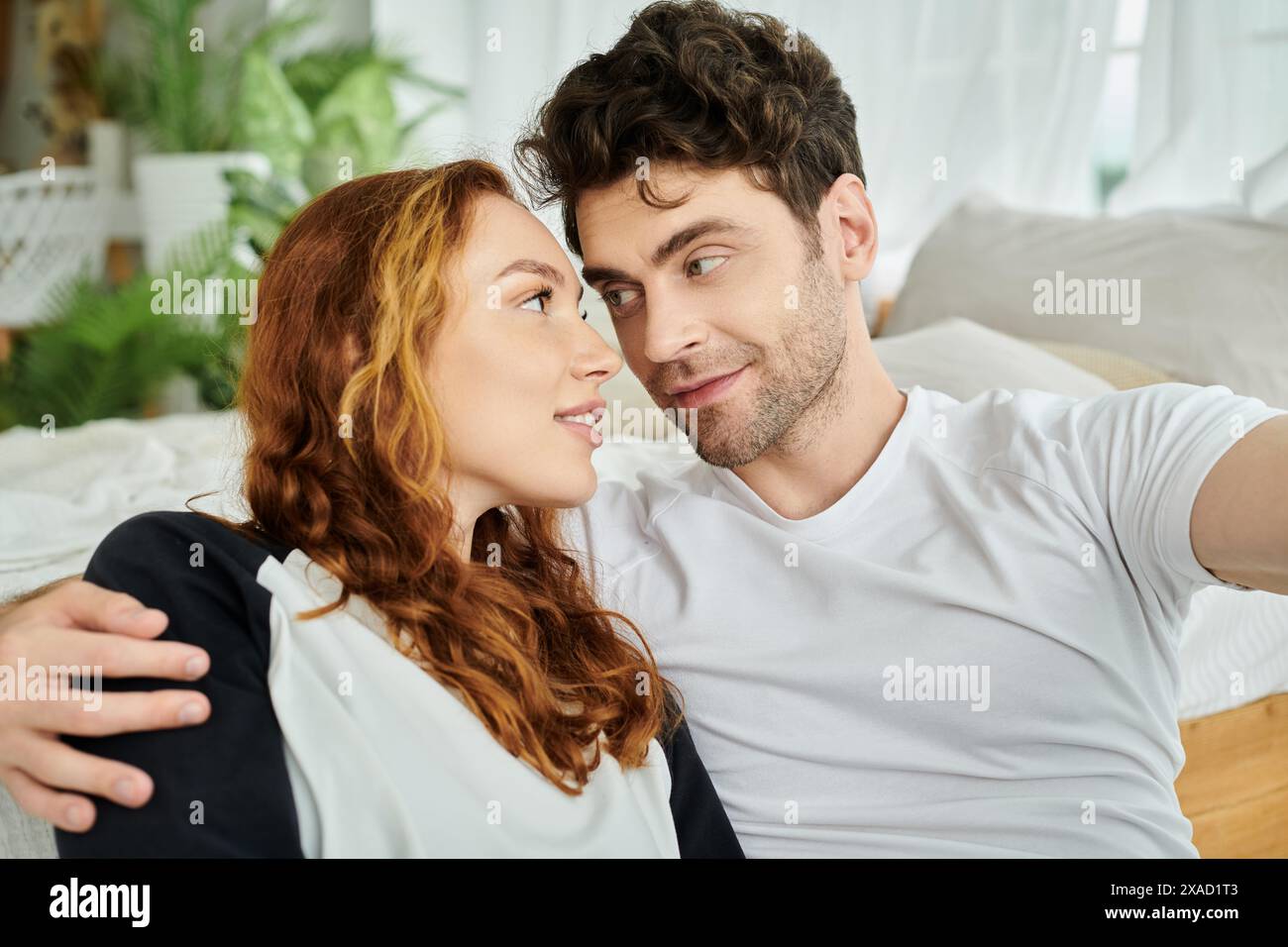 A man and a woman sitting on a bed, gazing at each other with a sense ...