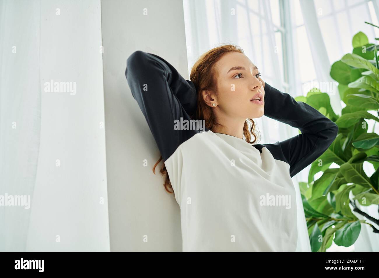 A woman leans against a wall with her hand on her head, lost in thought ...
