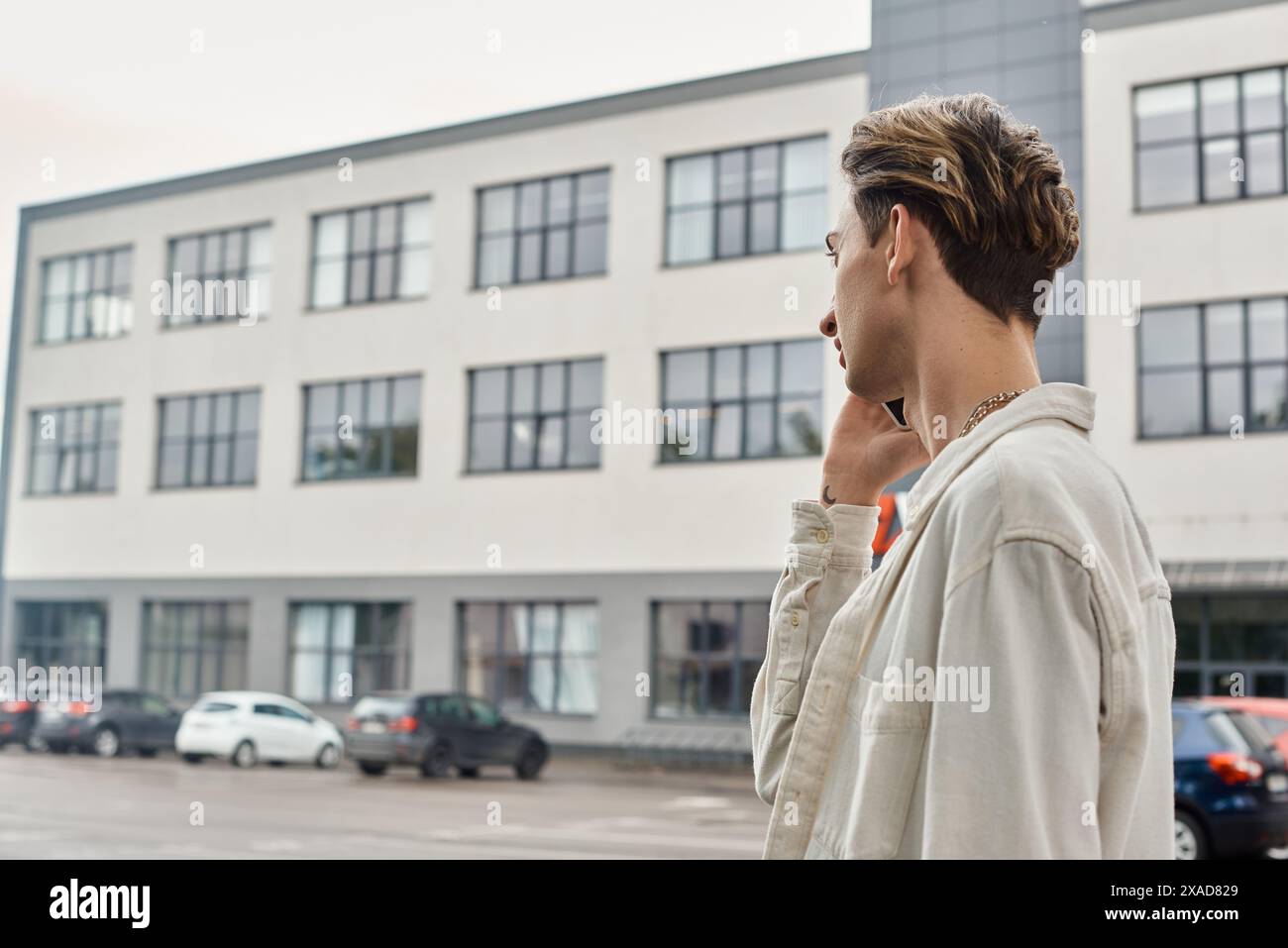 A young queer individual in fashionable attire talking on his cell ...