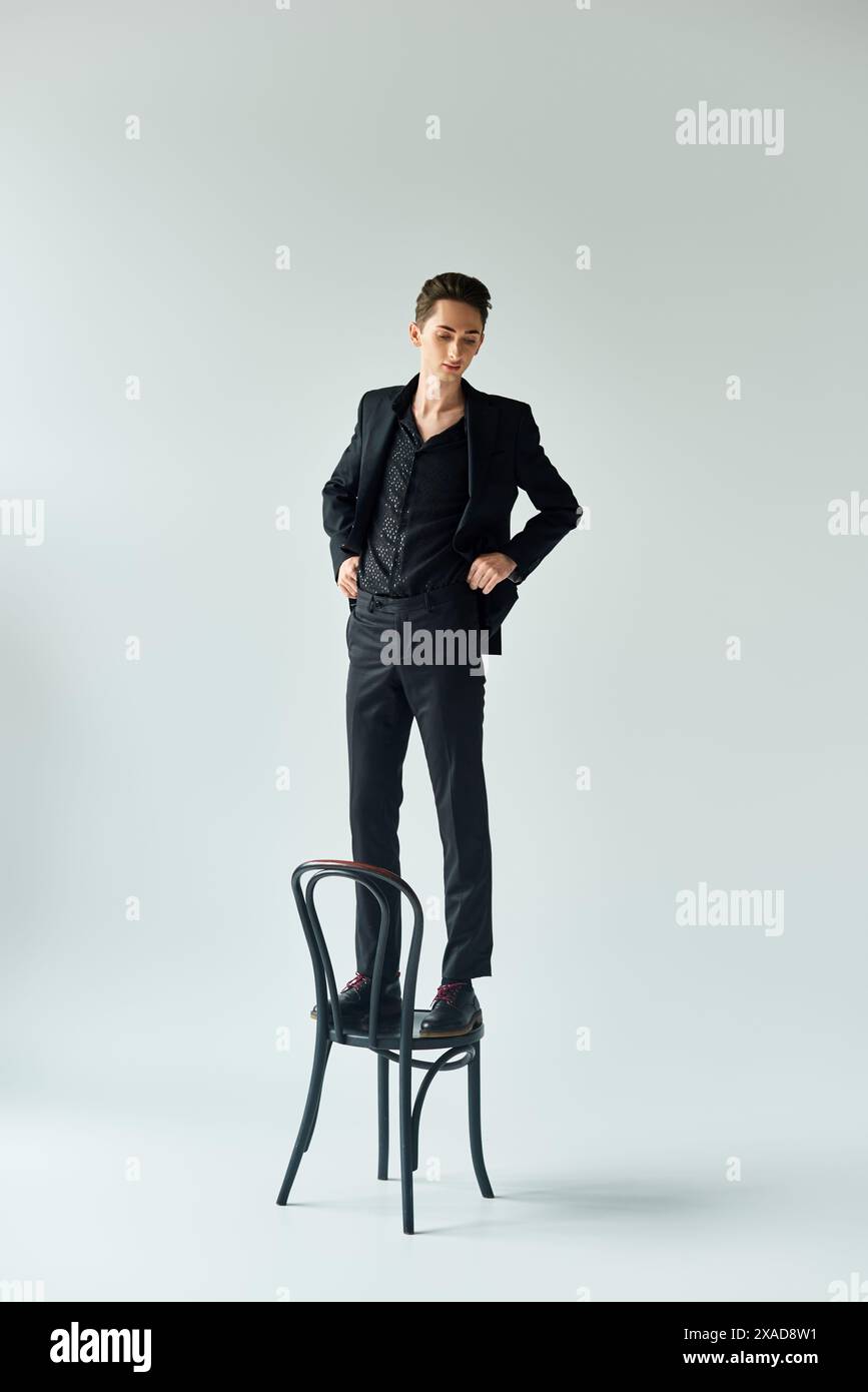 Stylish queer man in a black suit standing confidently on a chair in a ...