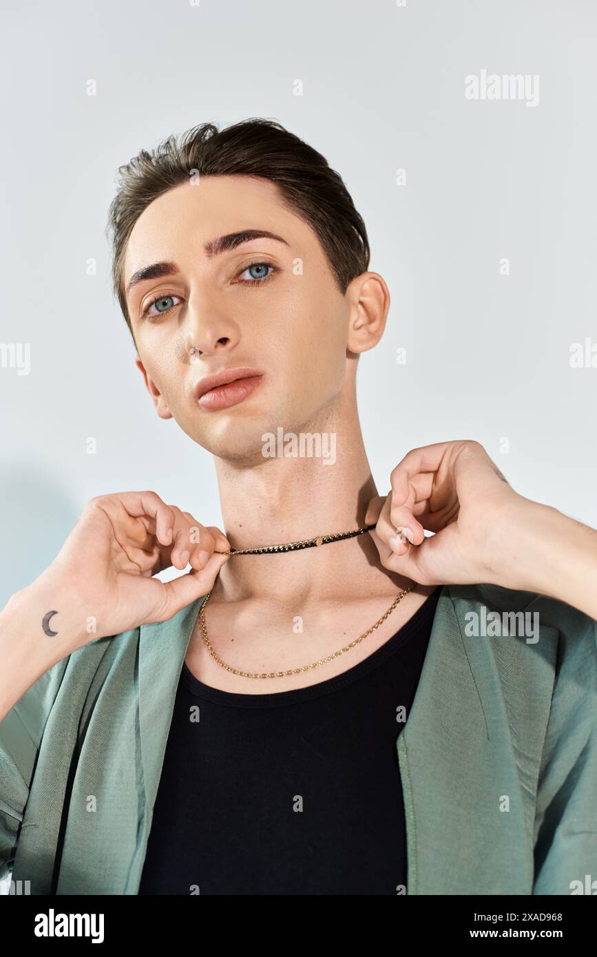 A young queer man adjusts his necklace, showcasing pride and elegance ...