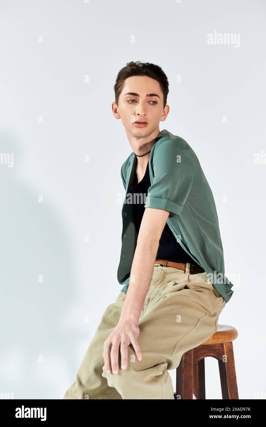 A young man confidently sits on a stool in a stylish green shirt and ...
