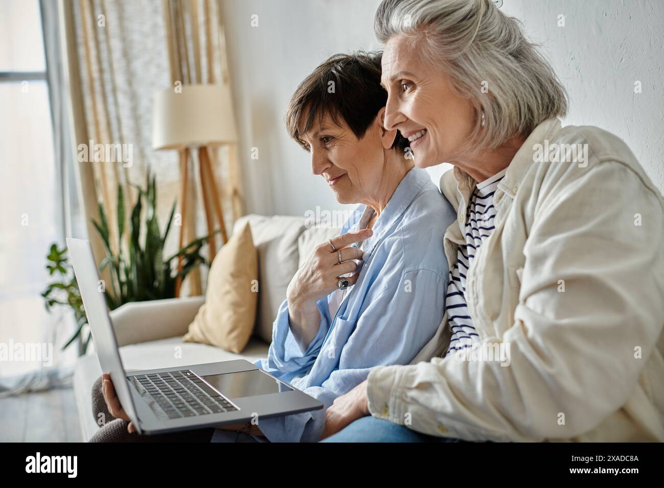 Two older women enjoy using a laptop while sitting on a couch together ...