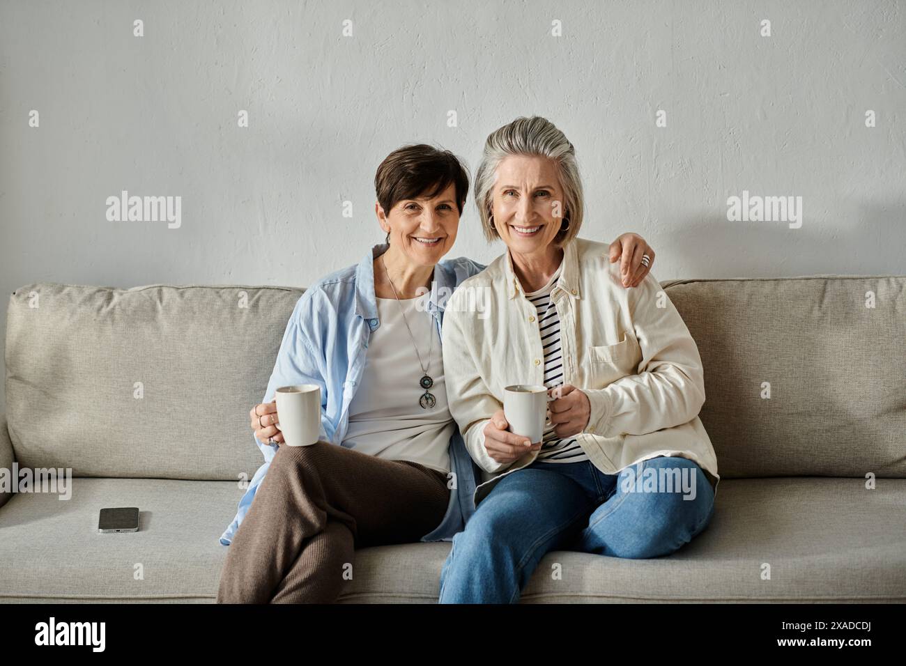 Two senior women relax on a couch, sipping coffee from mugs Stock Photo ...