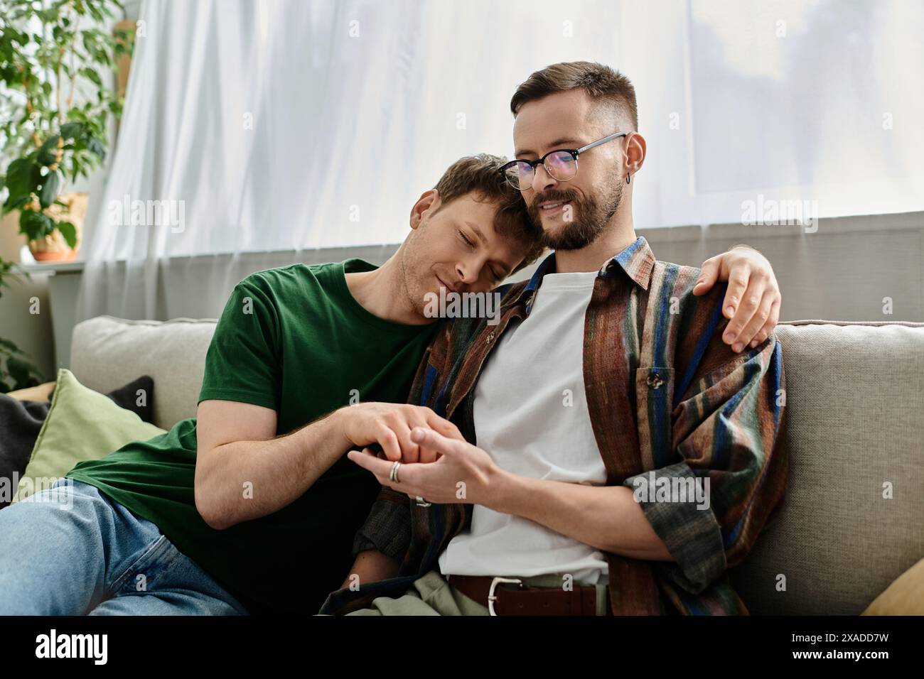 Two men in love in fashionable attire while sitting on top of a couch ...