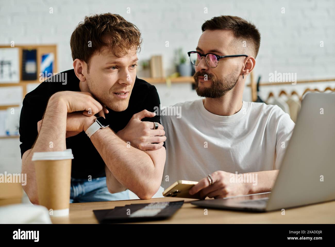 Two men, a gay couple, lean in towards a laptop screen, engrossed in ...