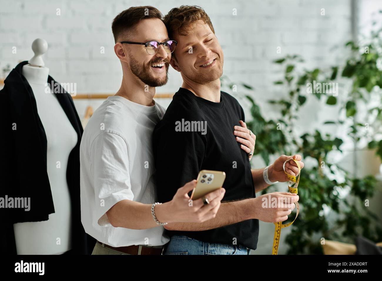 Two men, a gay couple, stand side by side working on trendy attire in their designer workshop ...