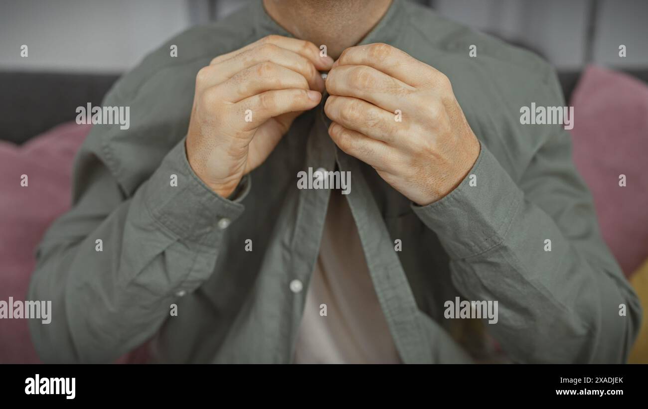 A handsome young man buttoning his shirt indoors, portraying daily life ...