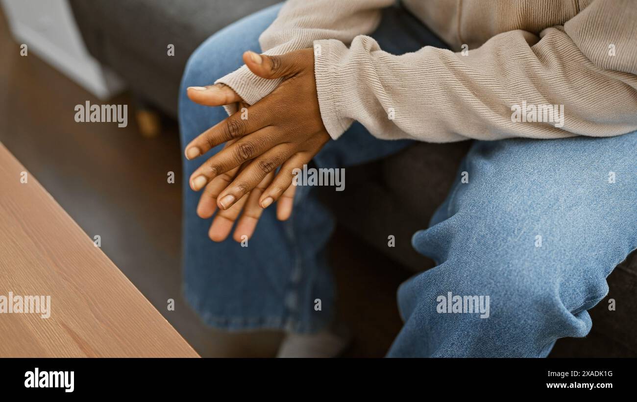 Casual african woman sitting thoughtfully at home, hands resting on ...
