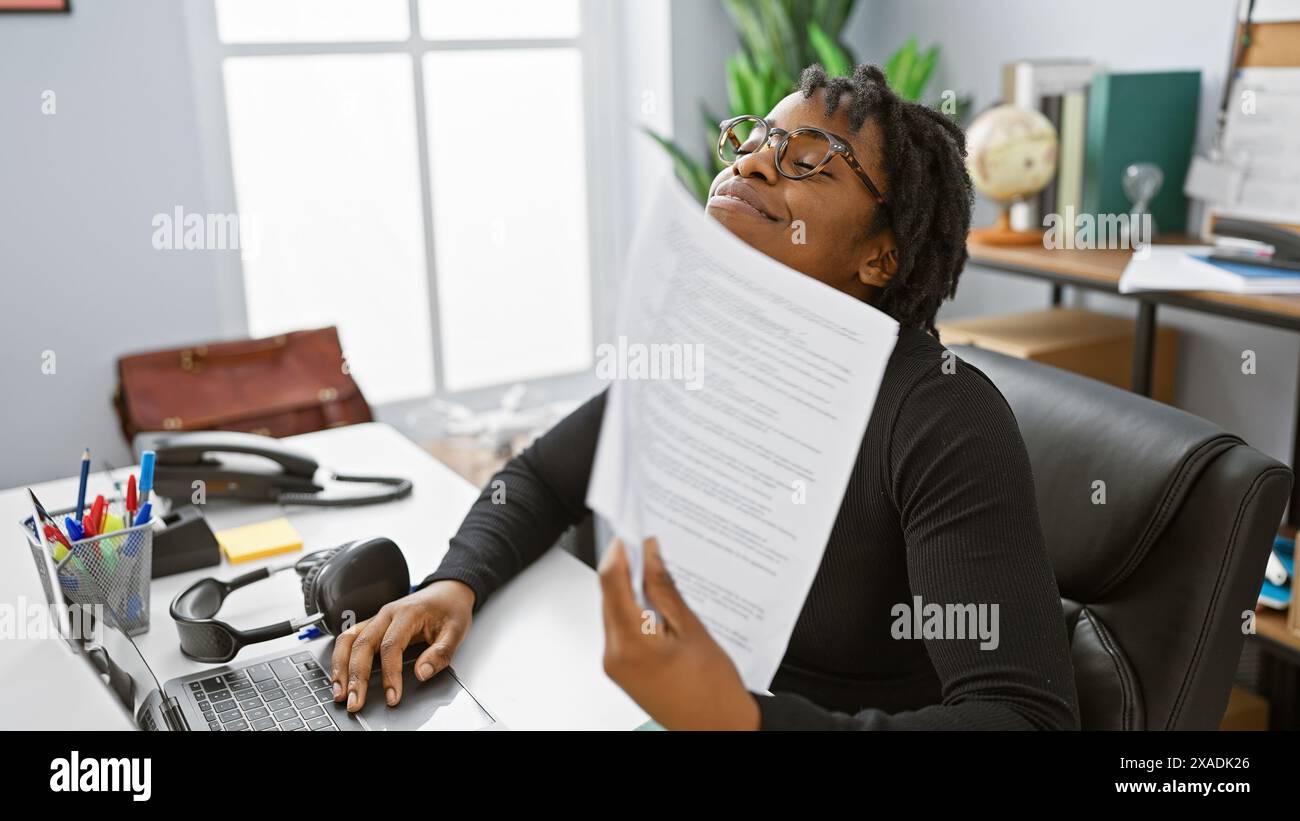 A young woman with dreadlocks in glasses fanning herself with a paper ...