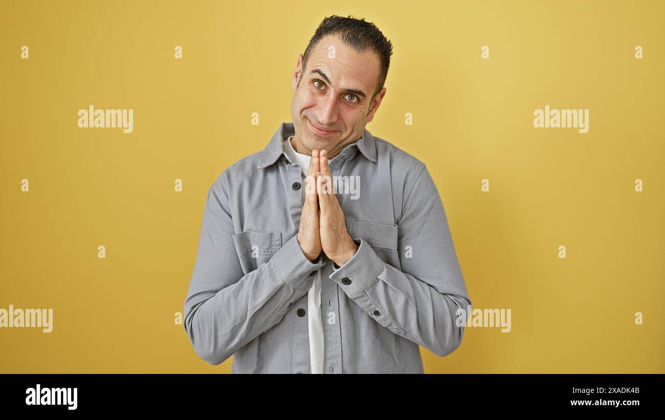 Hispanic man with a pleading expression standing against a yellow ...