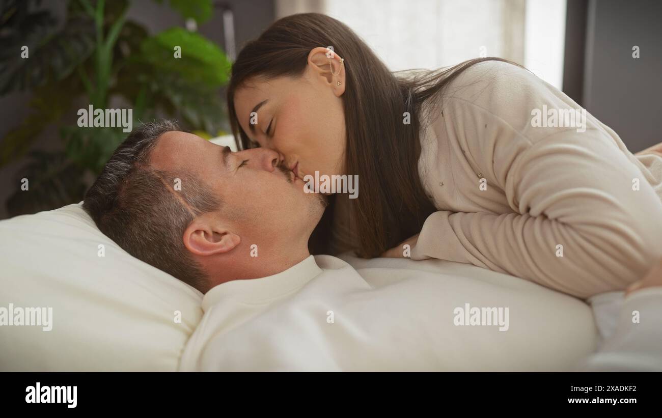 A loving couple affectionately kissing on a bed in a cozy bedroom, symbolizing relationship ...