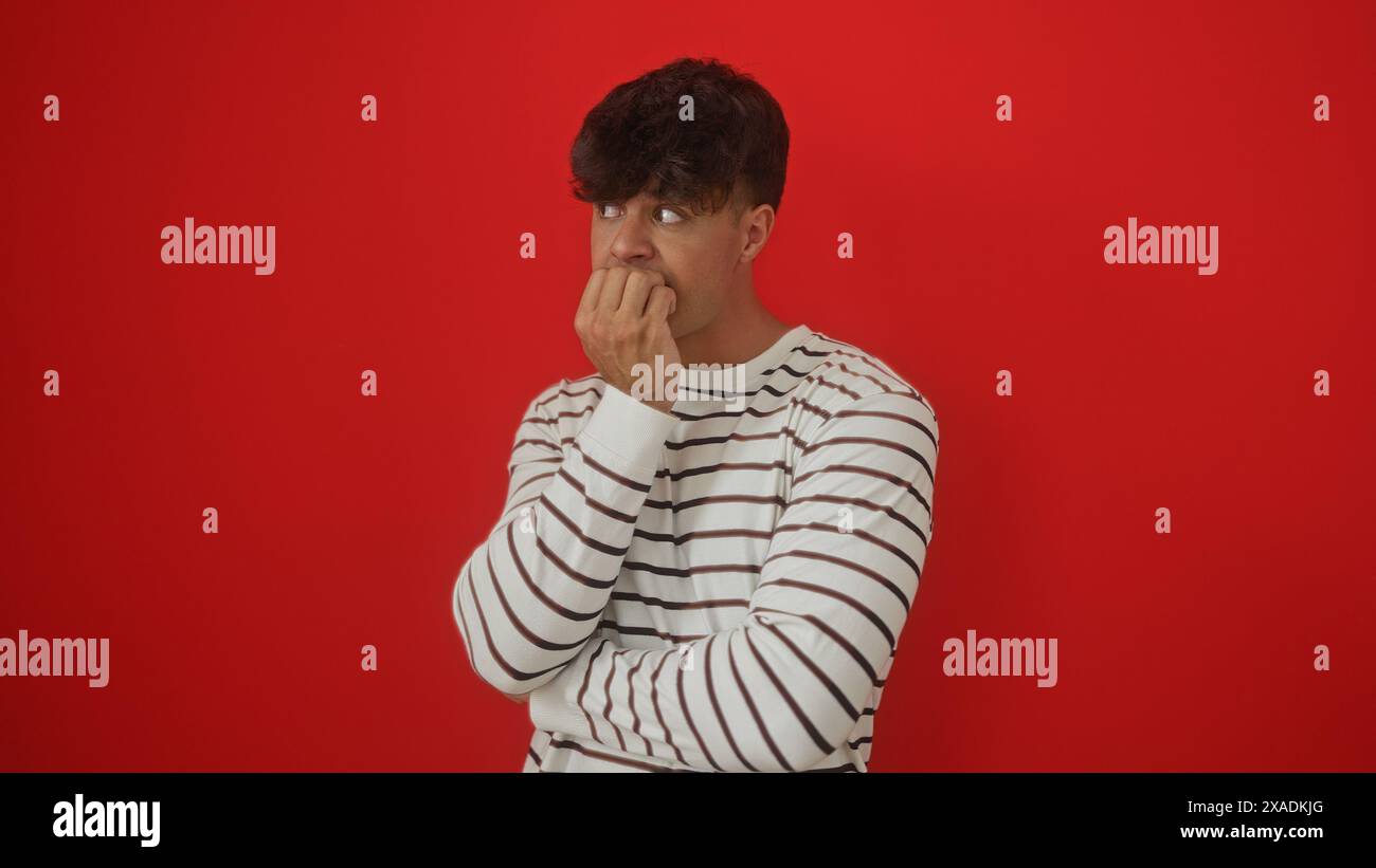 A young hispanic man poses thoughtfully against an isolated red ...