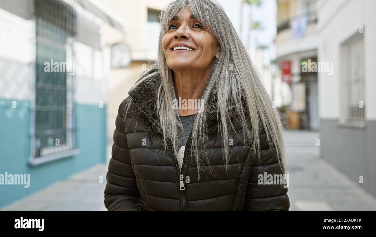 A mature woman with grey long hair smiles joyfully on an urban city ...
