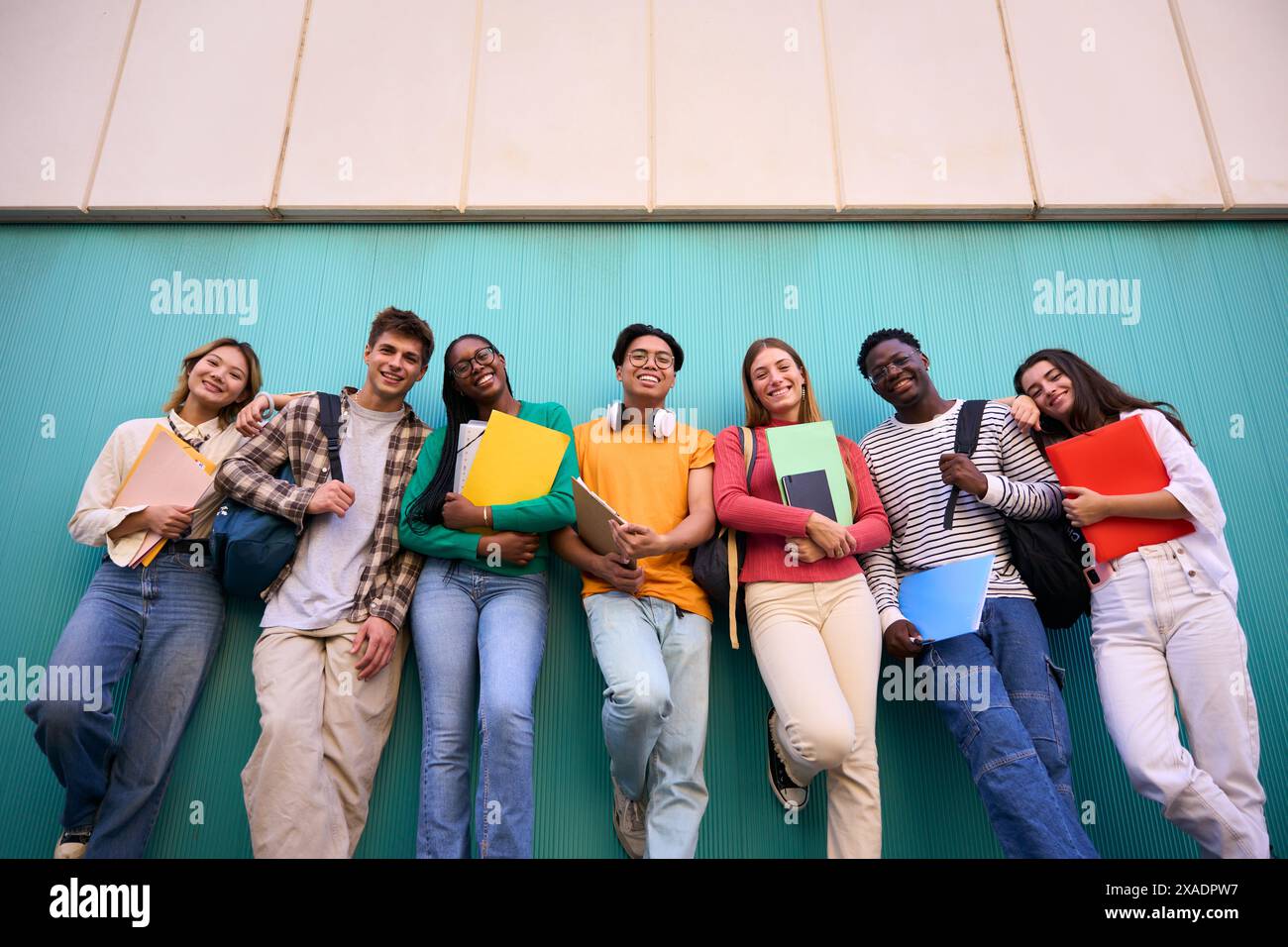 Low angle portrait of young multiracial students leaning against blue ...