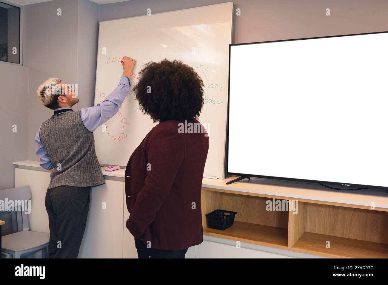 An Afro woman looking a man standing working in front of a whiteboard ...