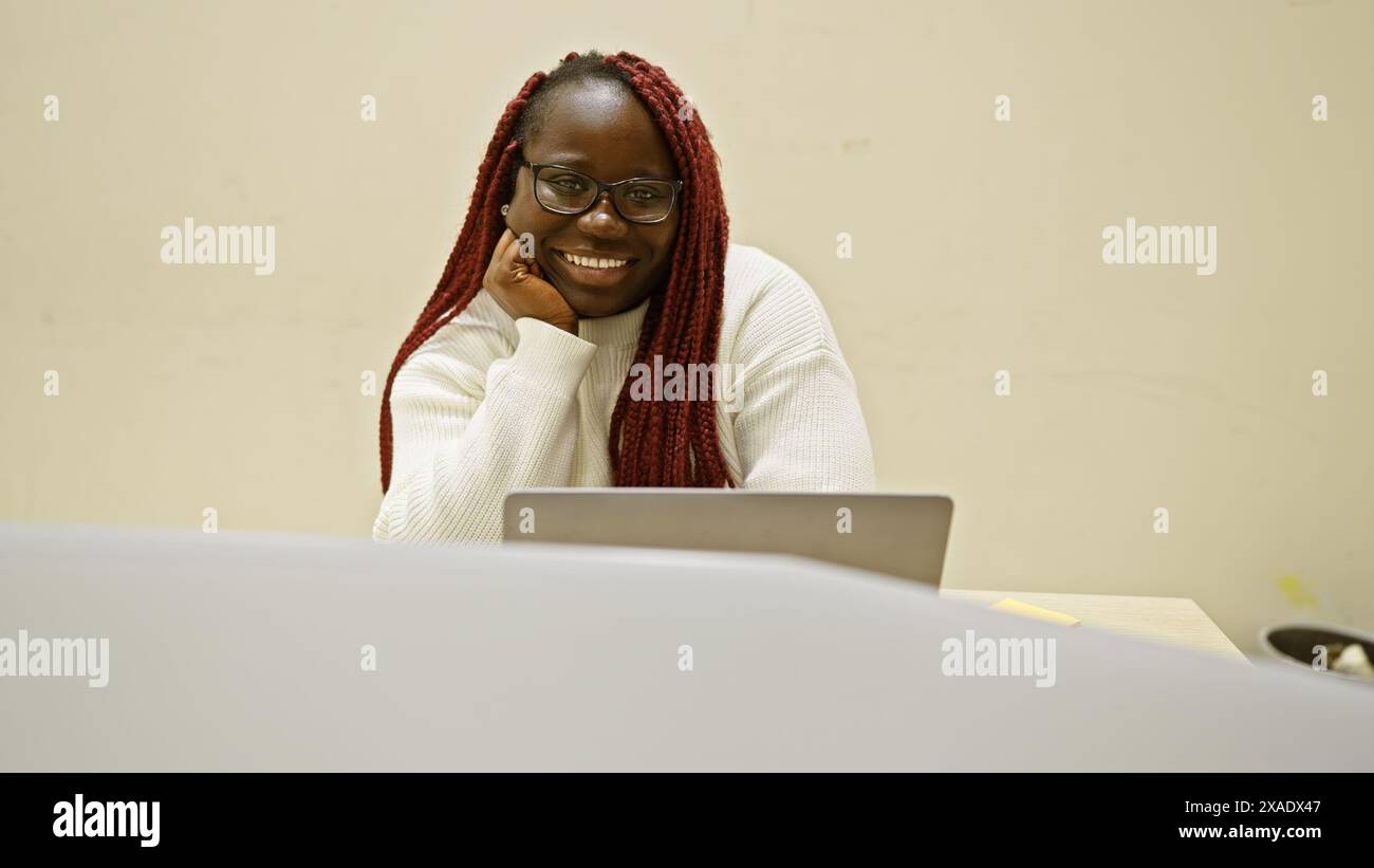 A smiling woman with red braids working indoors at an office, using a ...