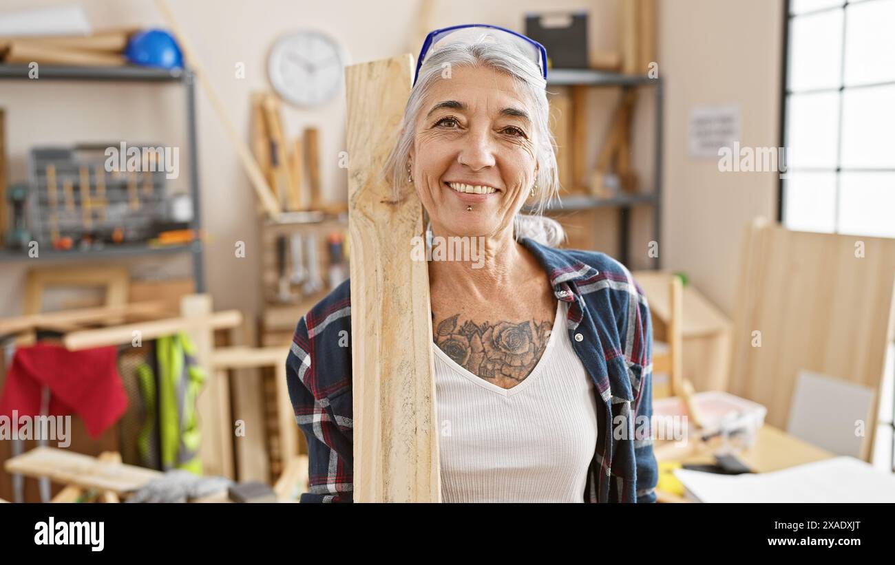 Smiling grey-haired middle age woman carpenter proudly holding a wood ...