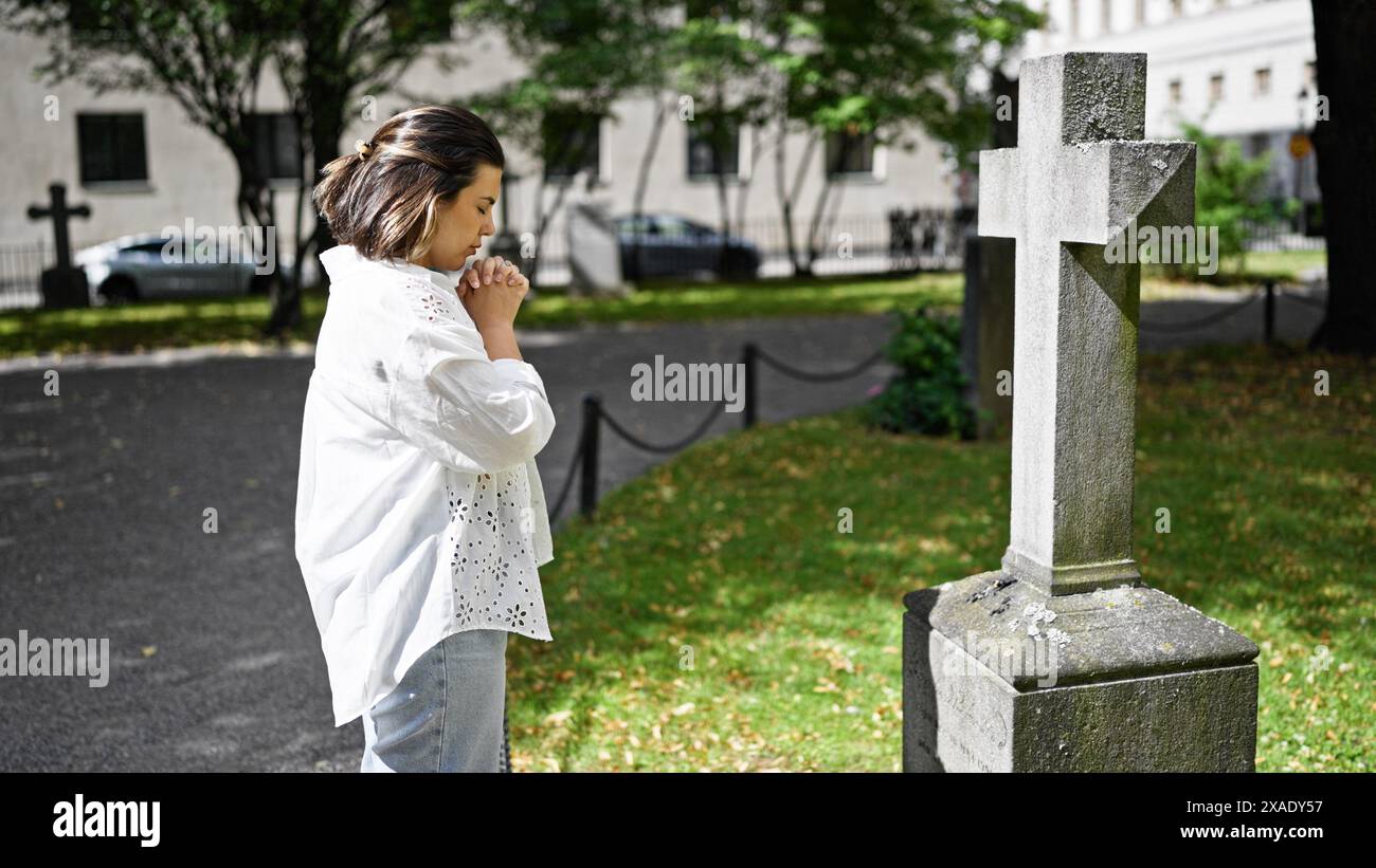 Beautiful young hispanic woman praying and mourning by tombstone at ...