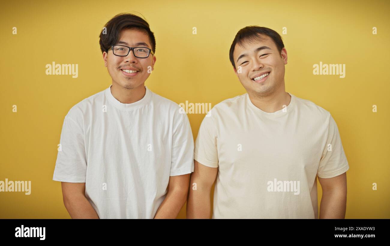 Two asian men smiling in casual attire against a yellow background ...