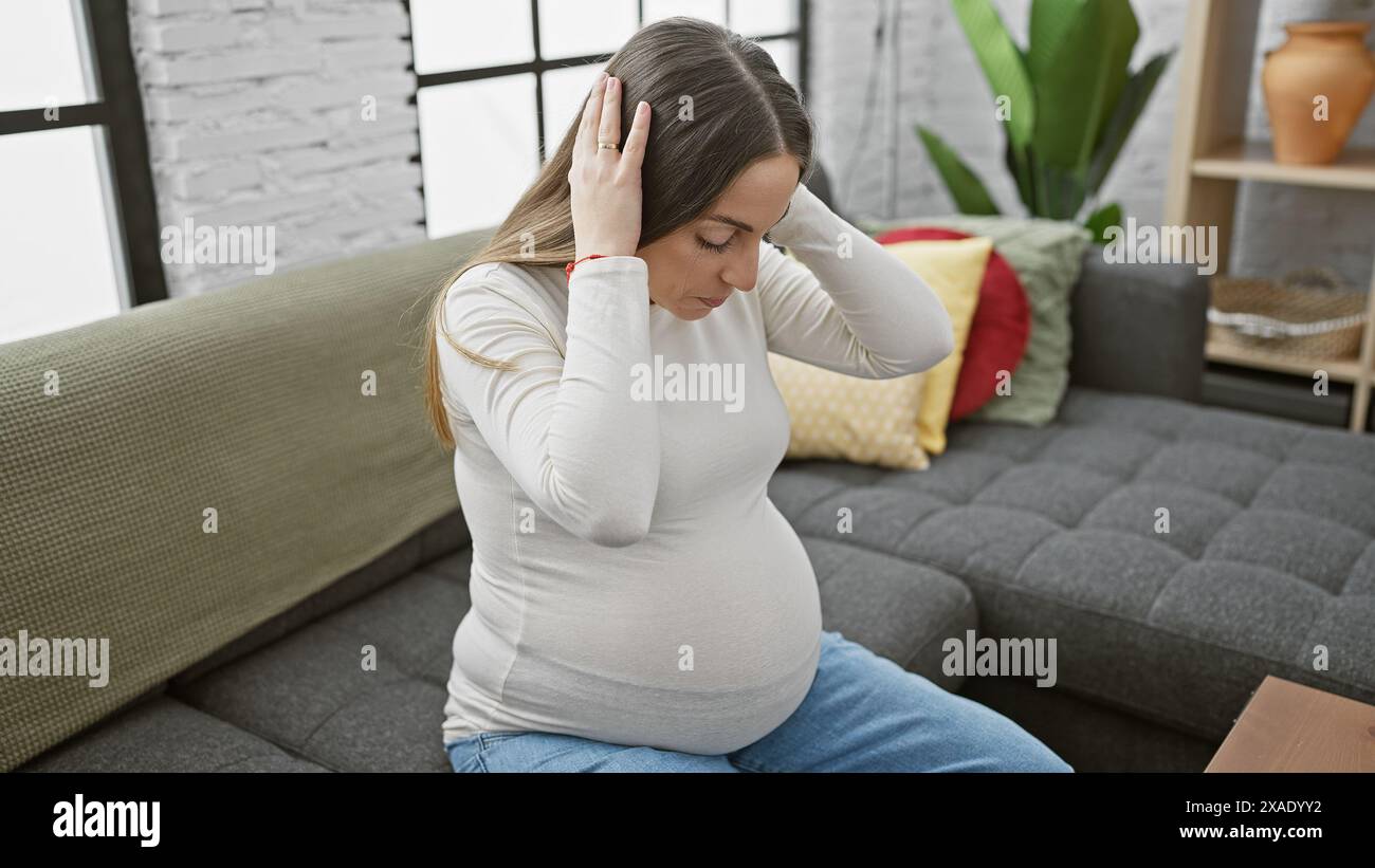 A distressed pregnant hispanic woman sitting on a gray couch indoors ...
