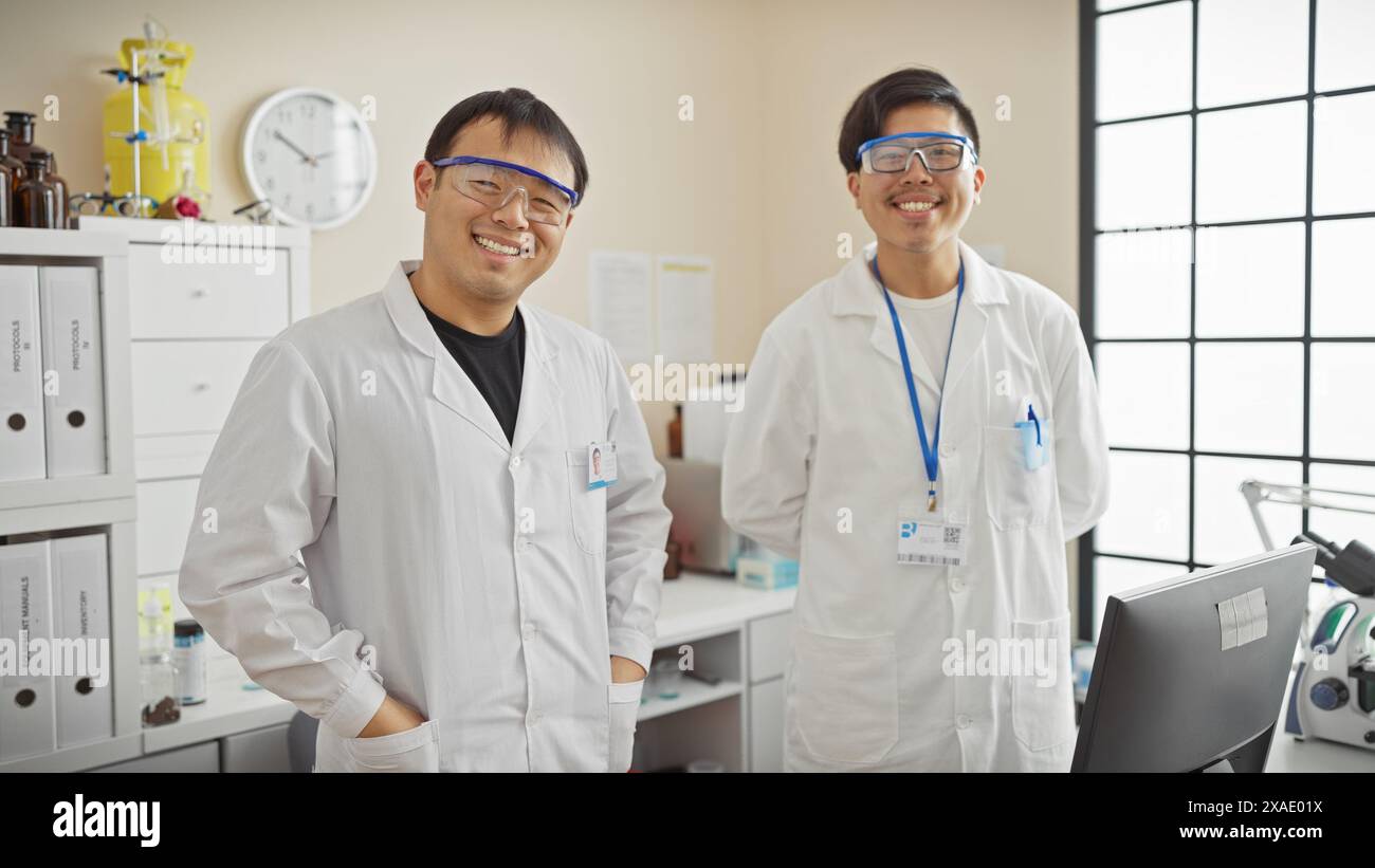 Two smiling men scientists in lab coats and safety glasses stand in a ...