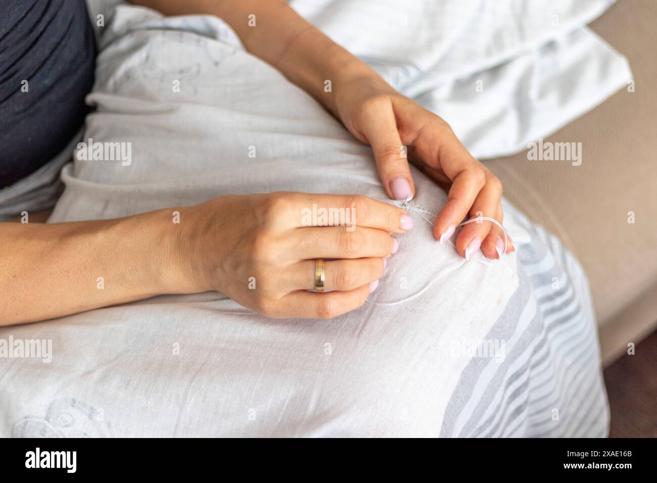 Shot of the woman with beautiful hands stitching up or patching a linen ...