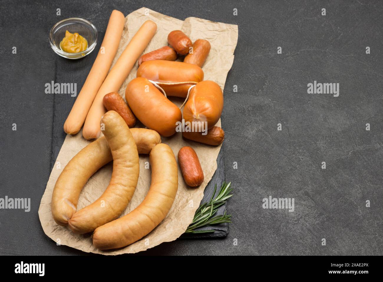 Sausages of different varieties on paper. Fork, mustard in glass bowl ...