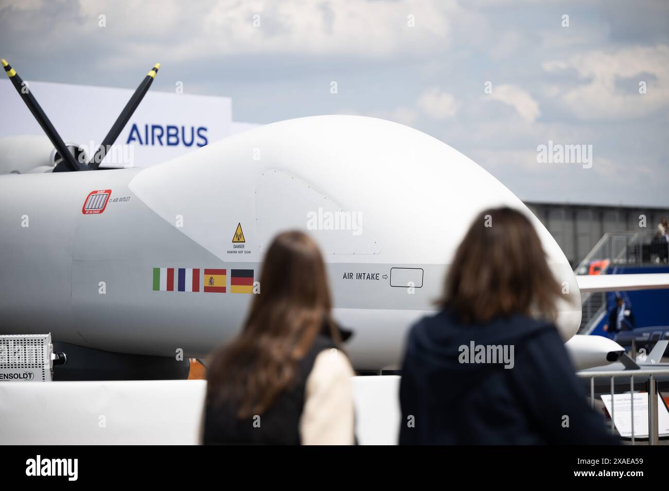06 June 2024, Brandenburg, Schönefeld: Two women walk past a model of the Airbus Eurodrone ...