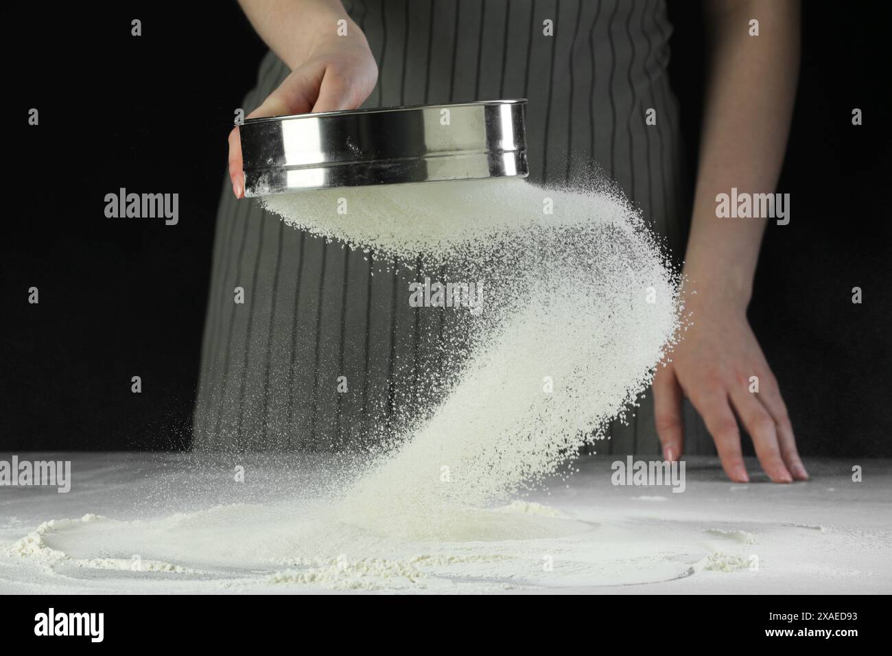 Woman sieving flour at table against black background, closeup Stock ...