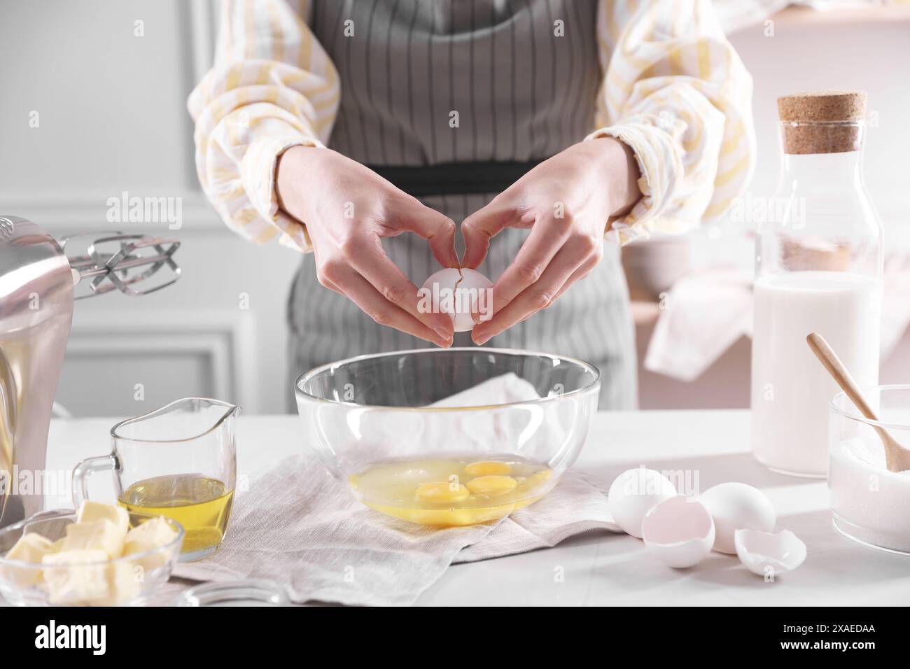 Making dough. Woman breaking egg at white table in kitchen, closeup Stock Photo - Alamy