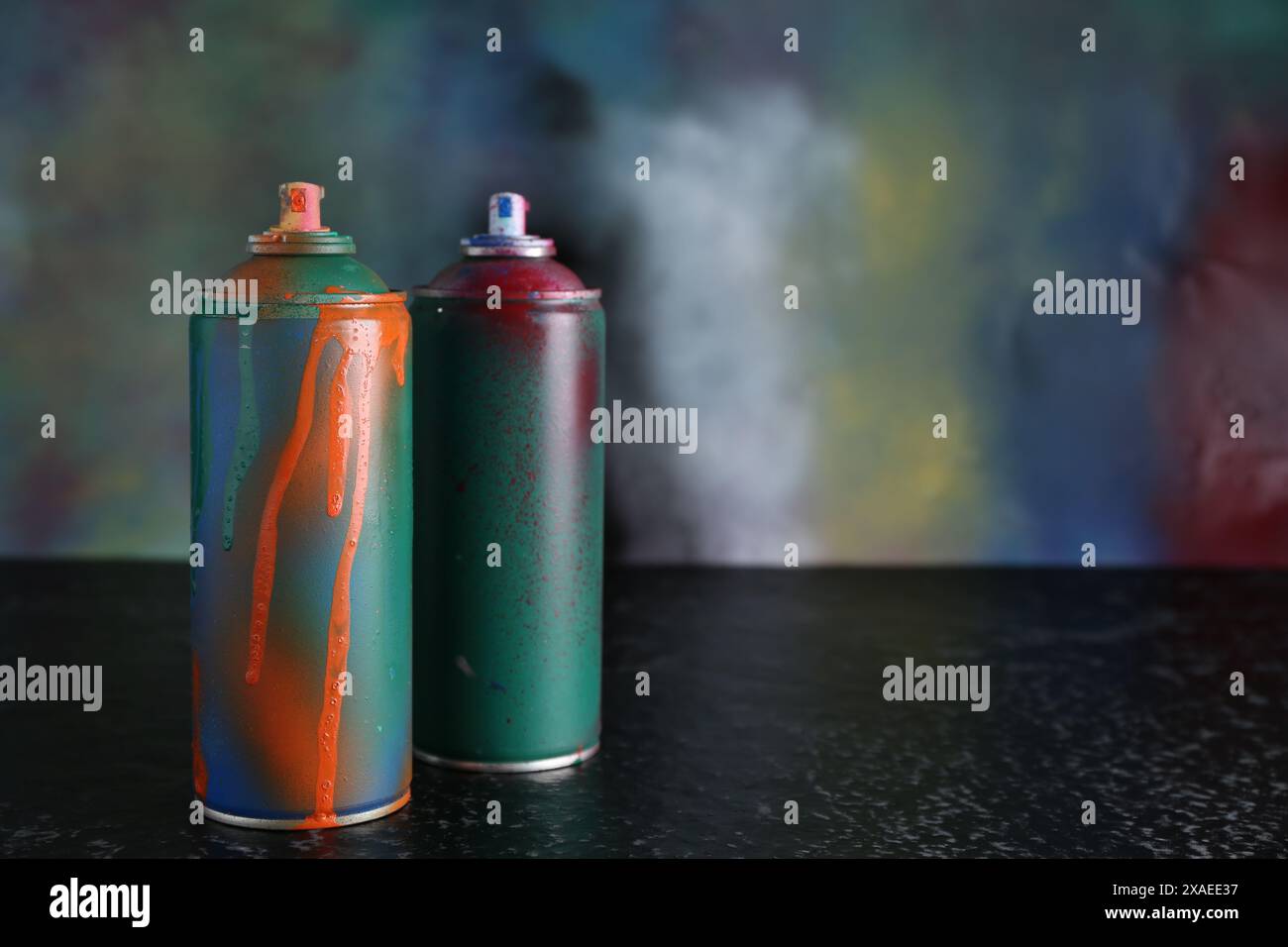 Two spray paint cans on black textured surface against color background ...