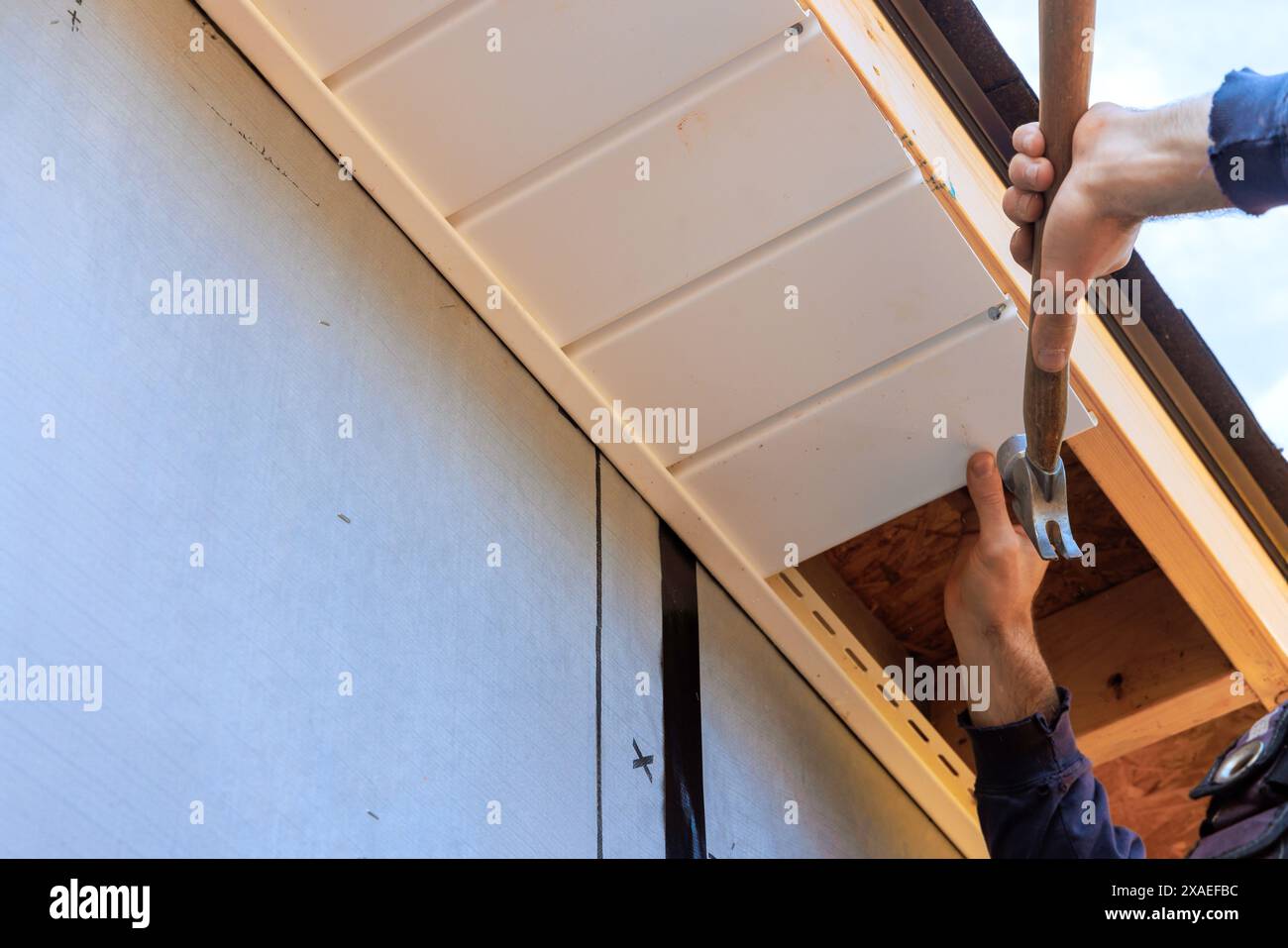 Worker installs plastic vinyl soffit at rooftop corner of rafters house ...