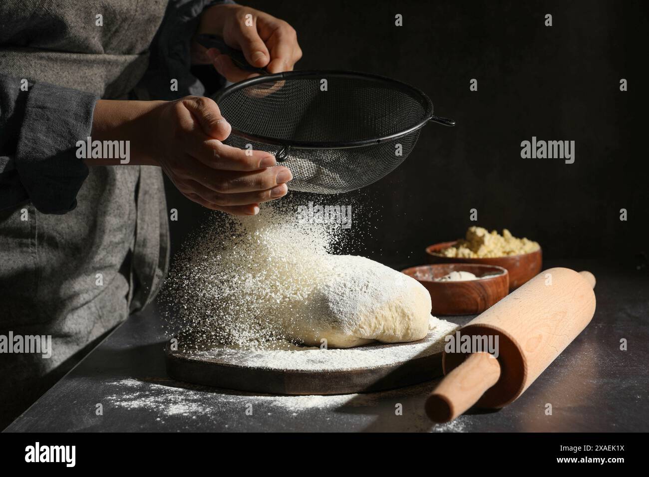 Woman sprinkling flour over dough at black table, closeup Stock Photo ...